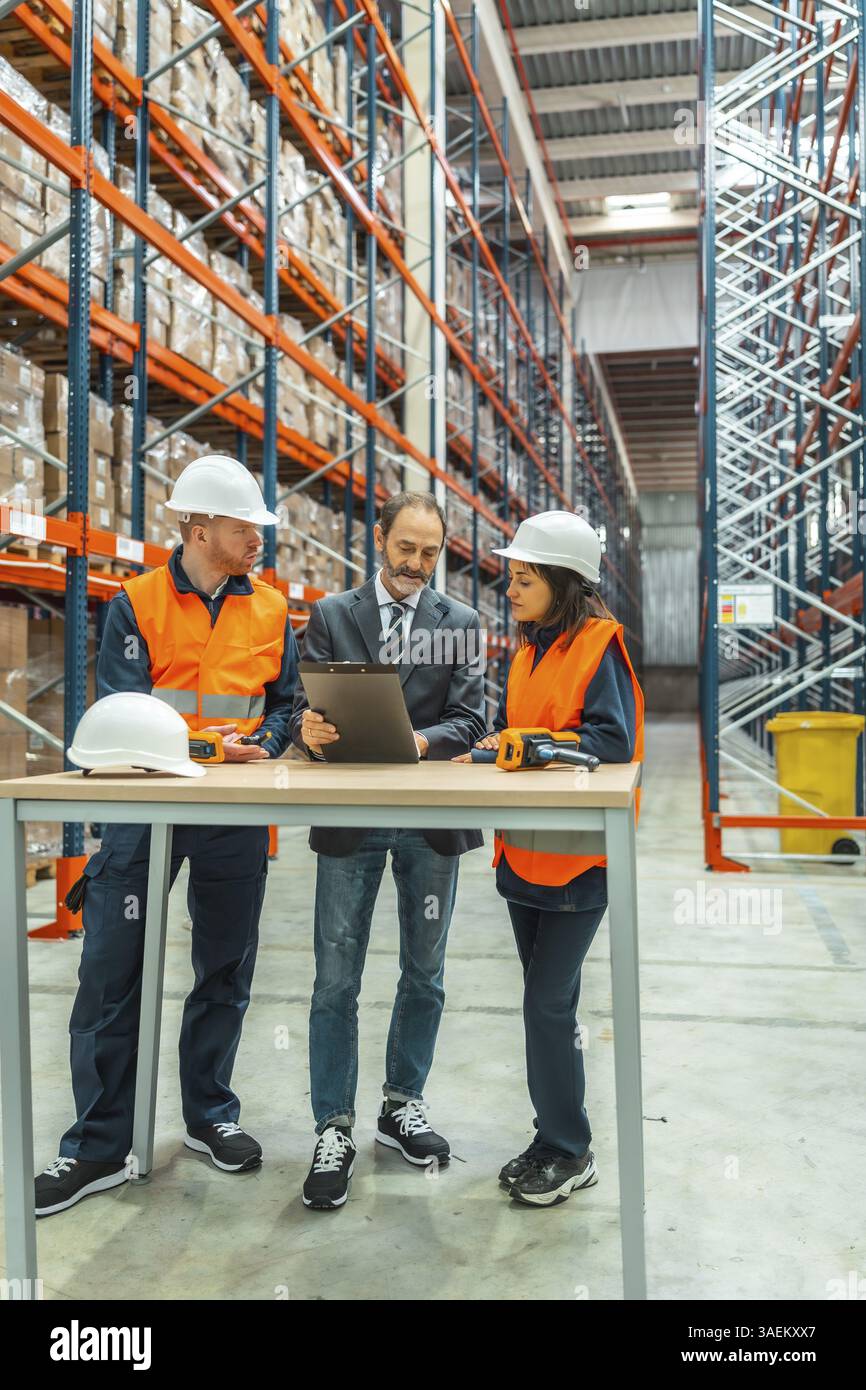 Manager holding clipboard showing inventory status to warehouse workers ...