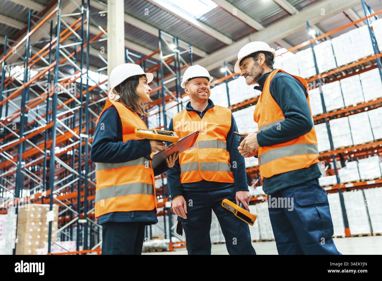 Warehouse workers wearing safety vests and helmets are discussing ...