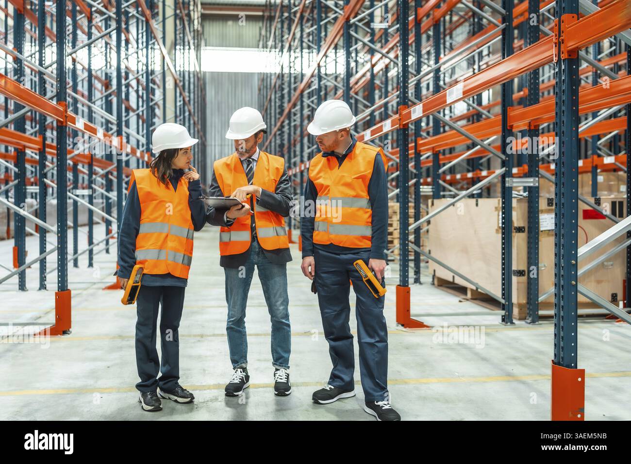 Warehouse workers wearing safety vests and hardhats are checking ...