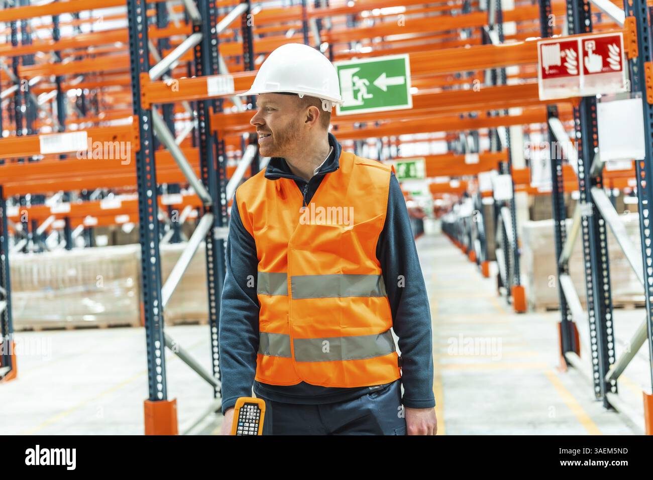 Warehouse worker wearing safety vest and helmet walking through ...