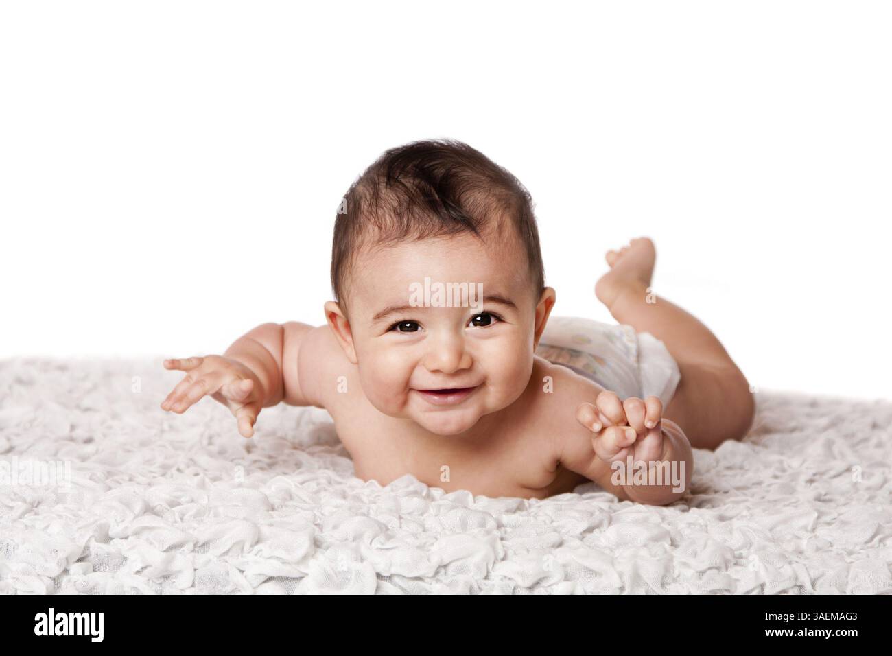 Cute happy smiling baby laying on belly on soft surface wearing diaper ...
