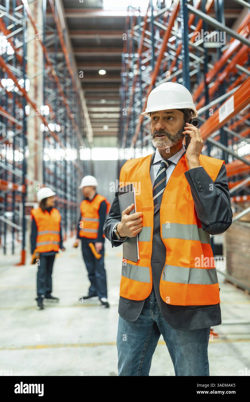 Warehouse manager wearing safety vest and helmet using phone and ...