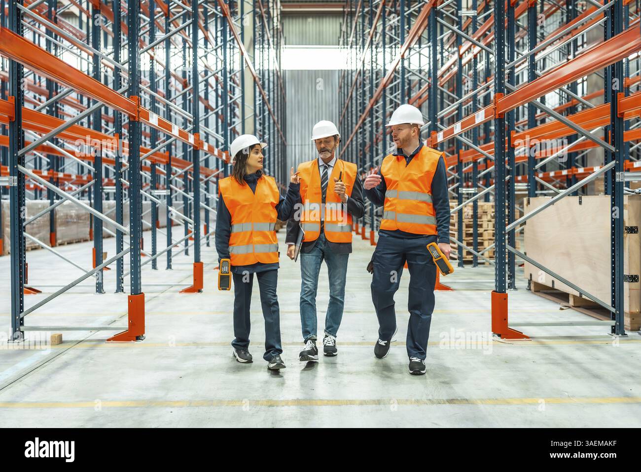Warehouse workers and manager walking through large distribution center ...