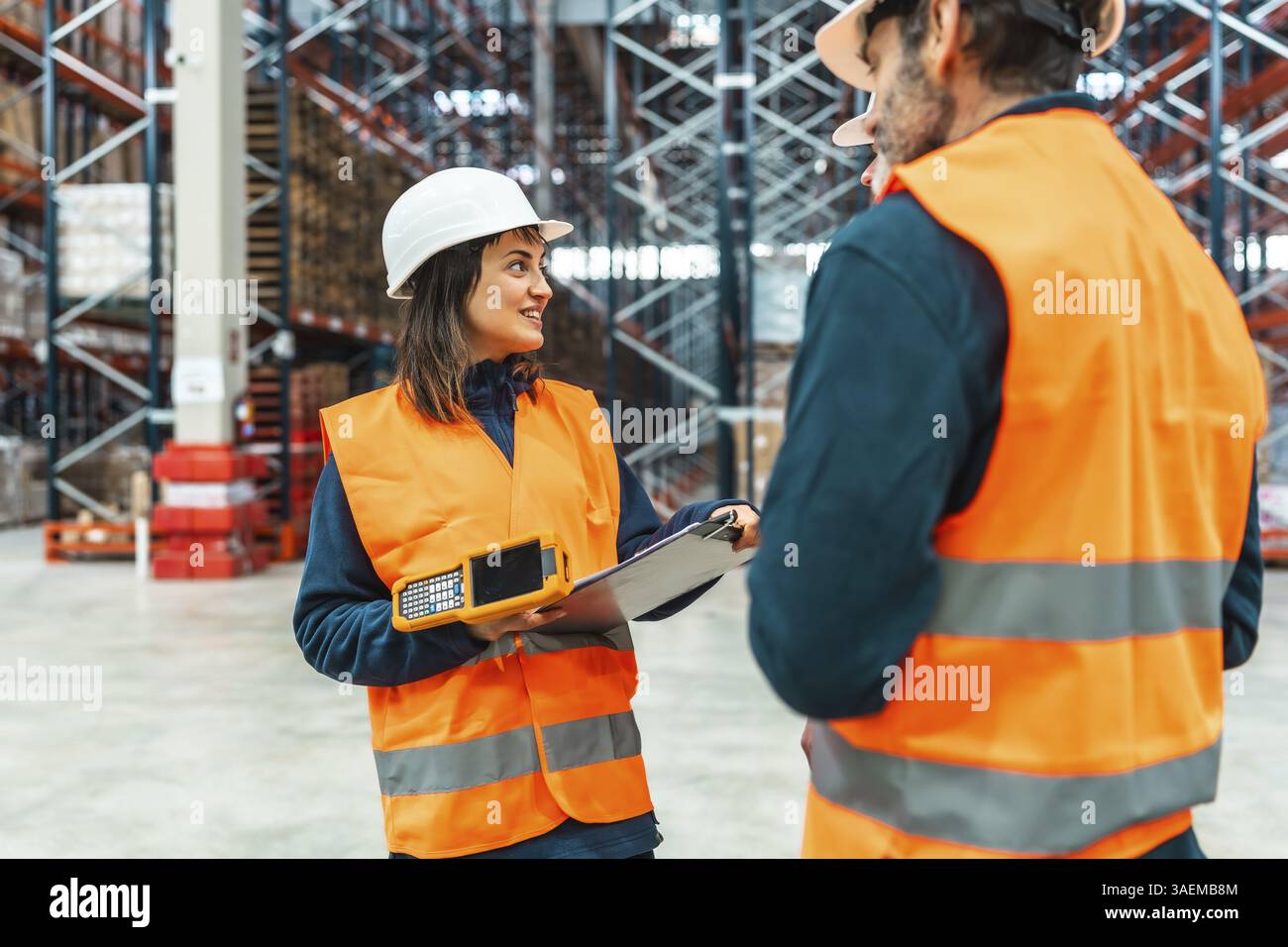 Two warehouse workers are discussing logistics, holding a handheld ...