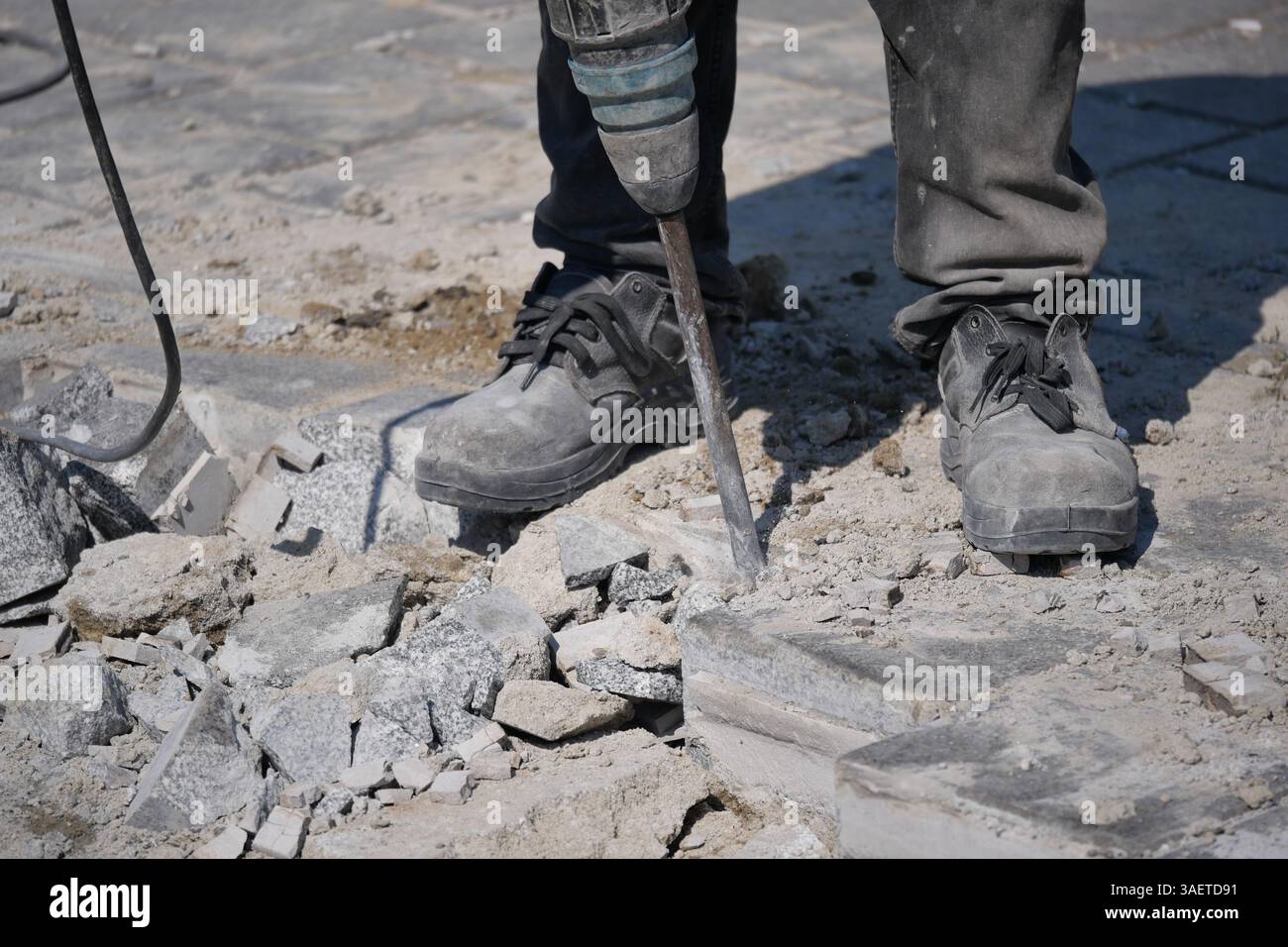 Worker using pneumatic tool to break concrete at construction site ...