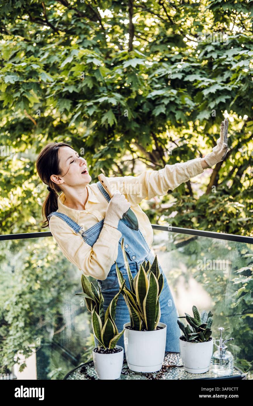 Young Asian woman playfully singing into a garden trowel while caring ...