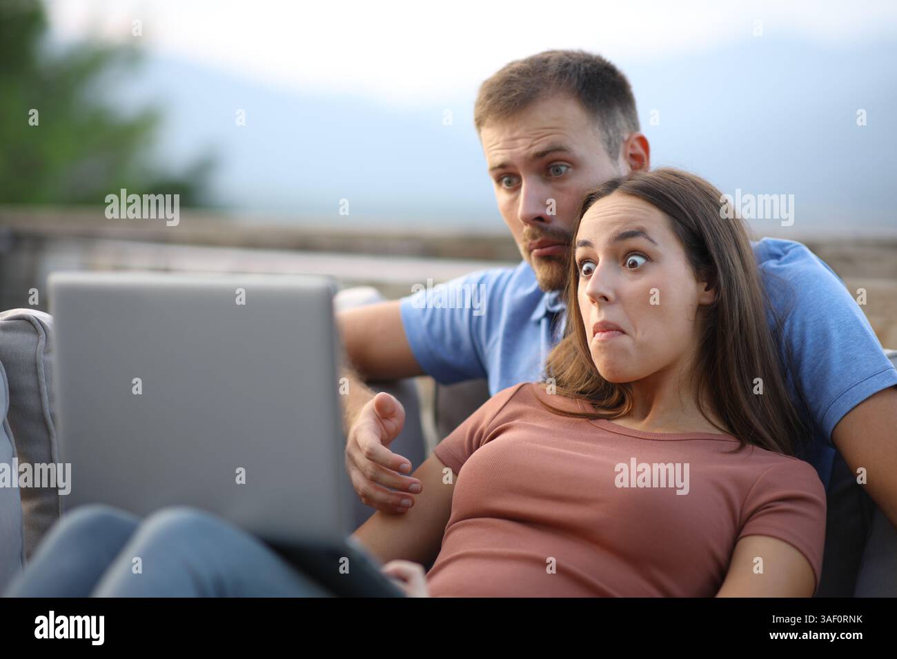 Confused couple watching media content on laptop sitting in a terrace ...