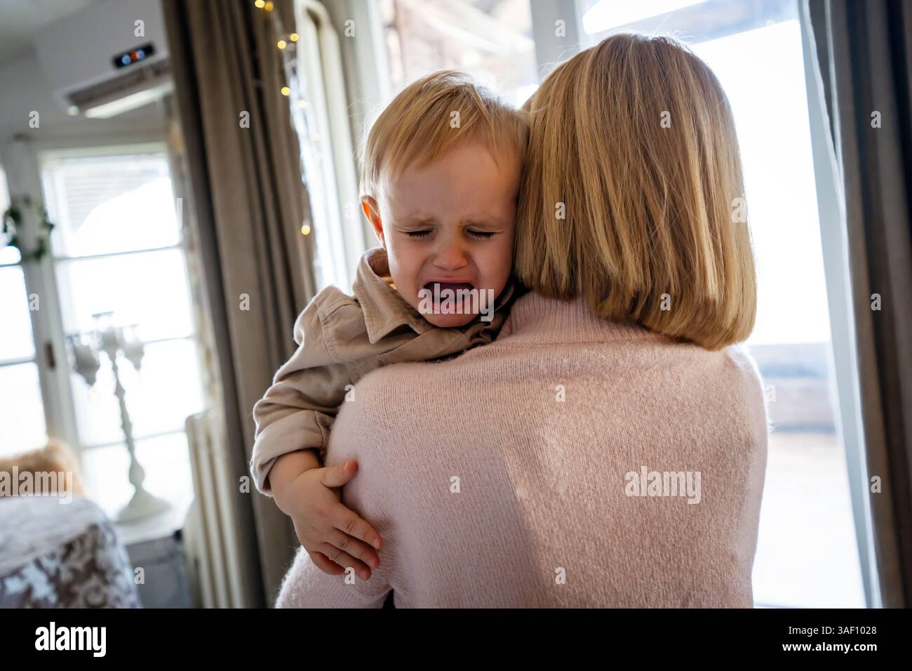 Mother soothes her crying child while carrying him at home. Kid is ...