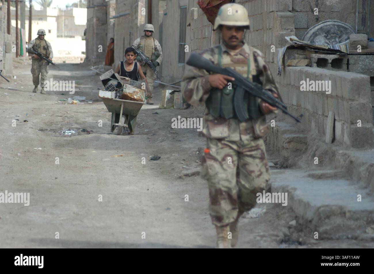 Apr 17, 2005; Ar Ramadi, Iraq; An Iraqi boy pushes a wheelbarrow behind ...