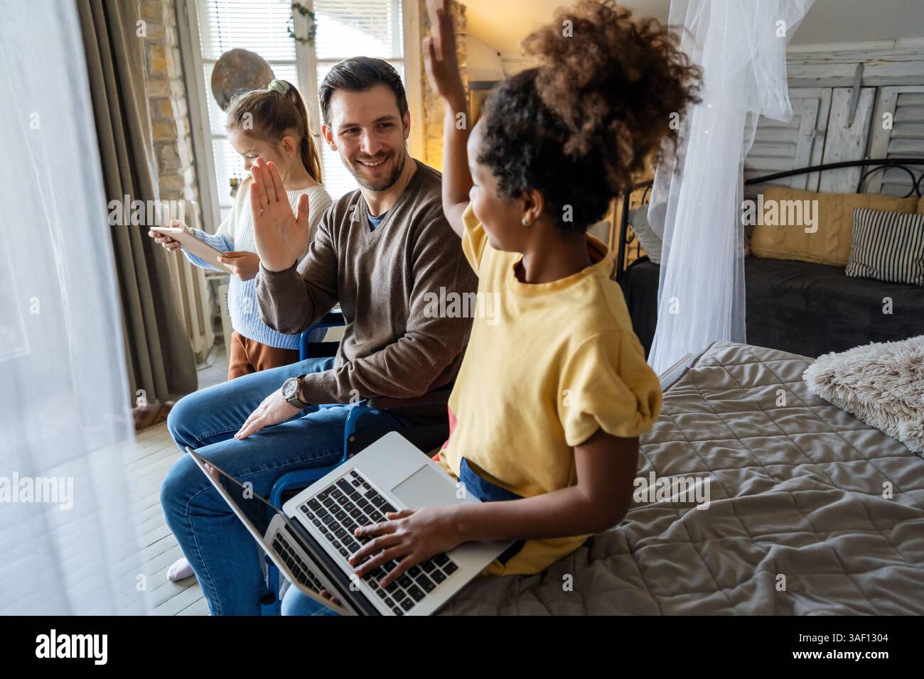 Happy father in wheelchair with interracial daughters using laptop together, education, fun ...