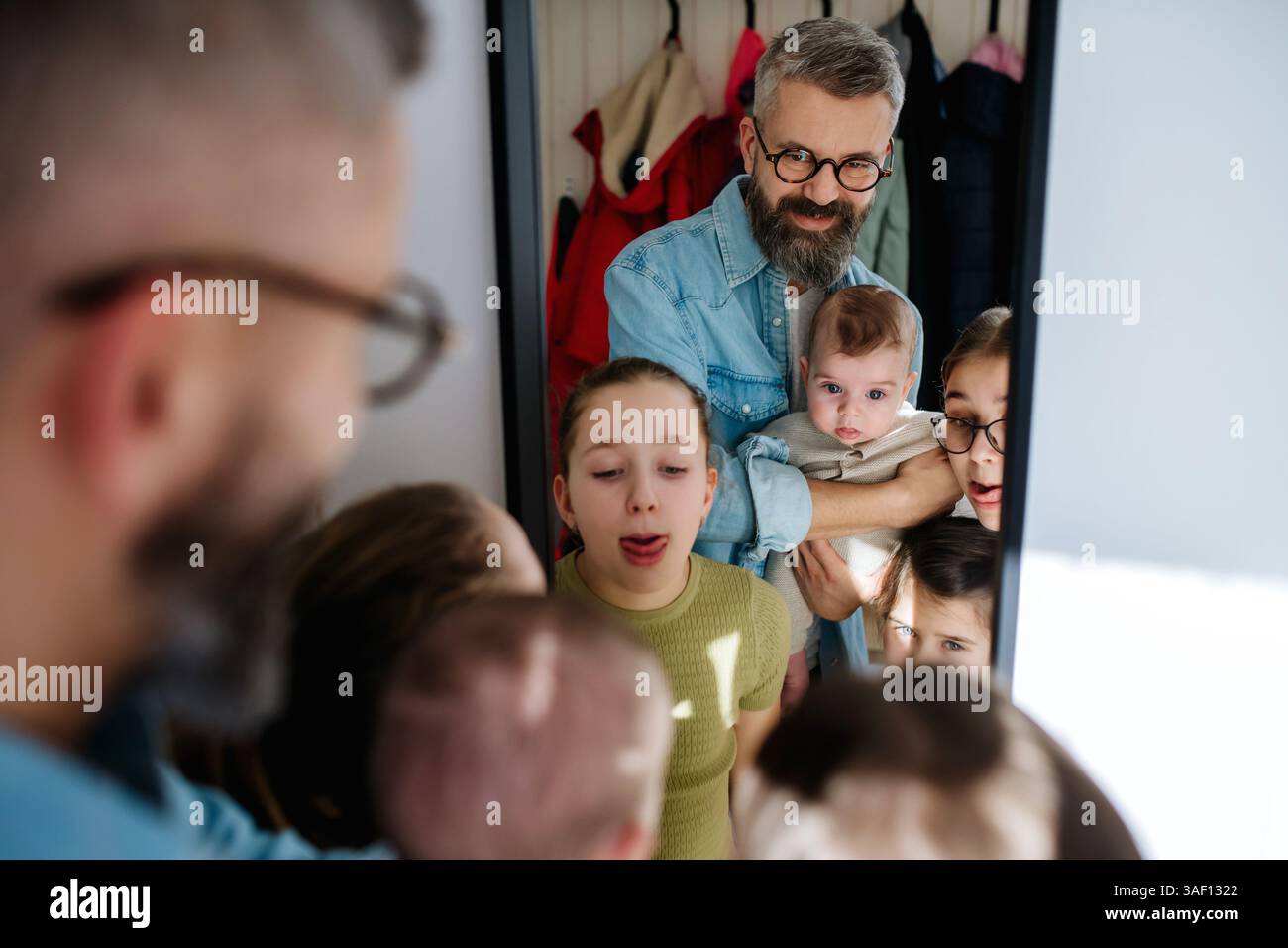 Three sisters, father and newborn brother looking in mirror Stock Photo ...
