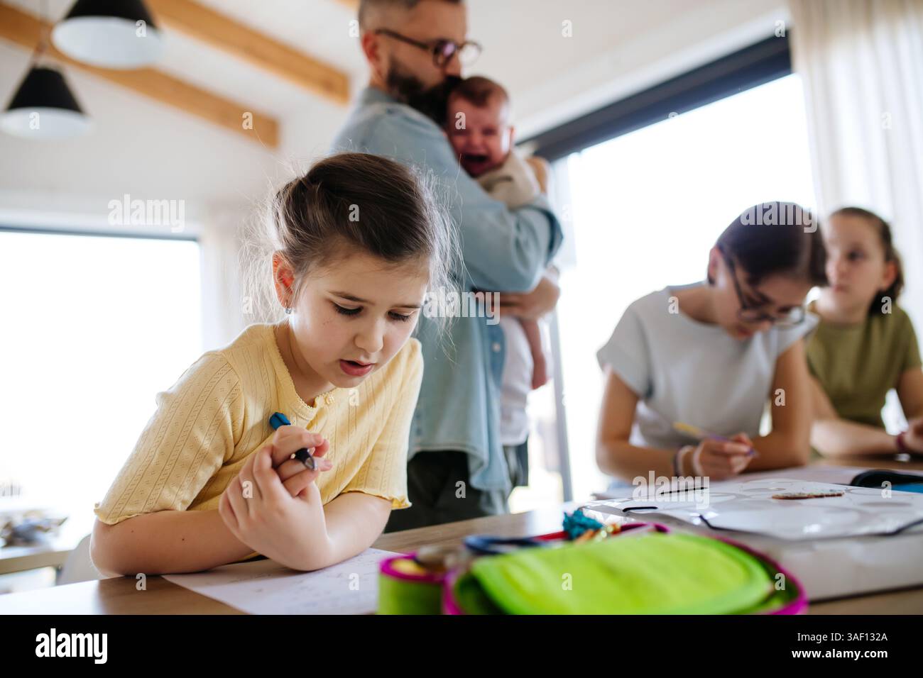 Father helping his daughters with homework while taking care of baby ...