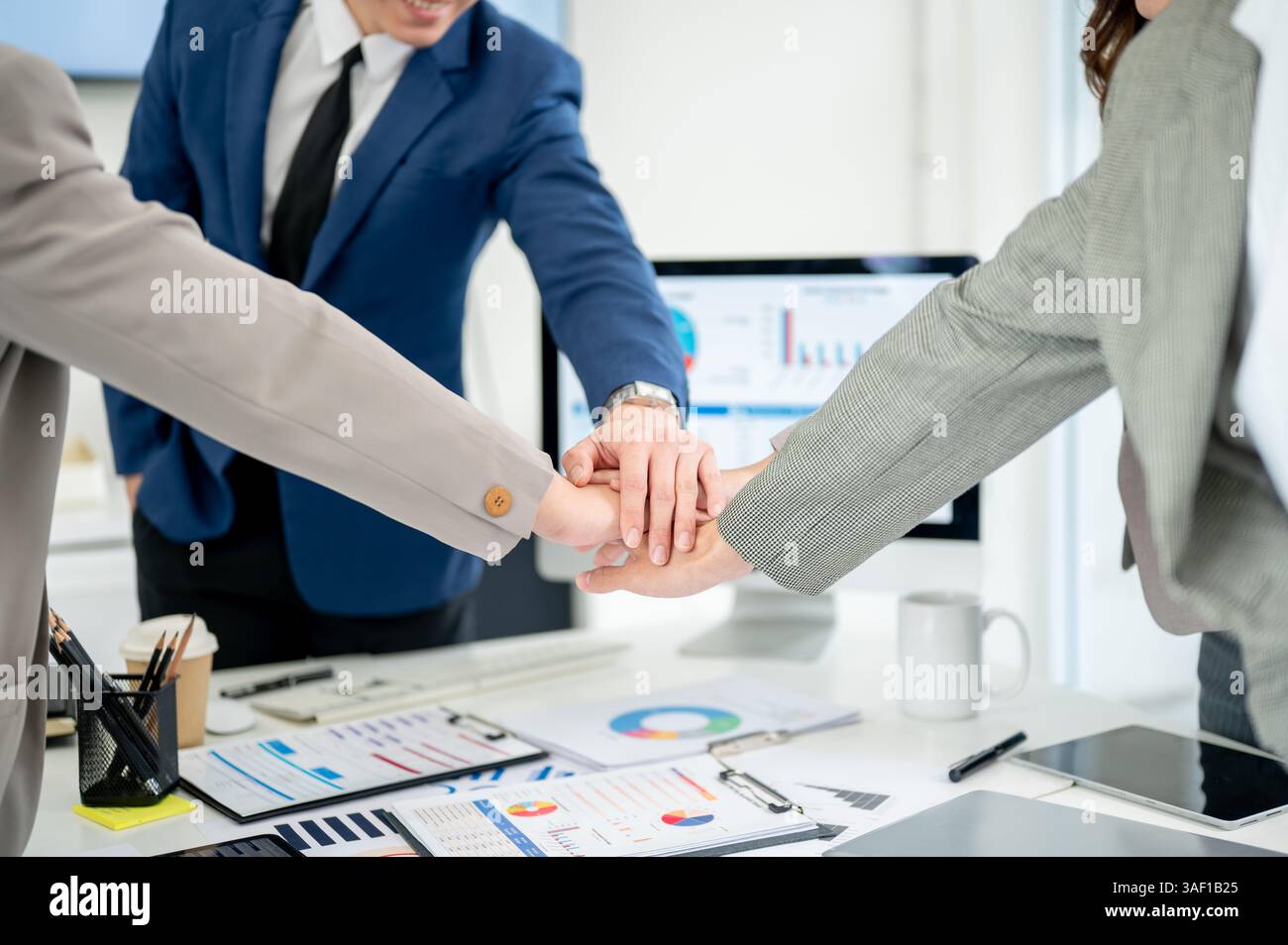 Side view of businessman and woman or office workers joining hands over the table with scattered ...