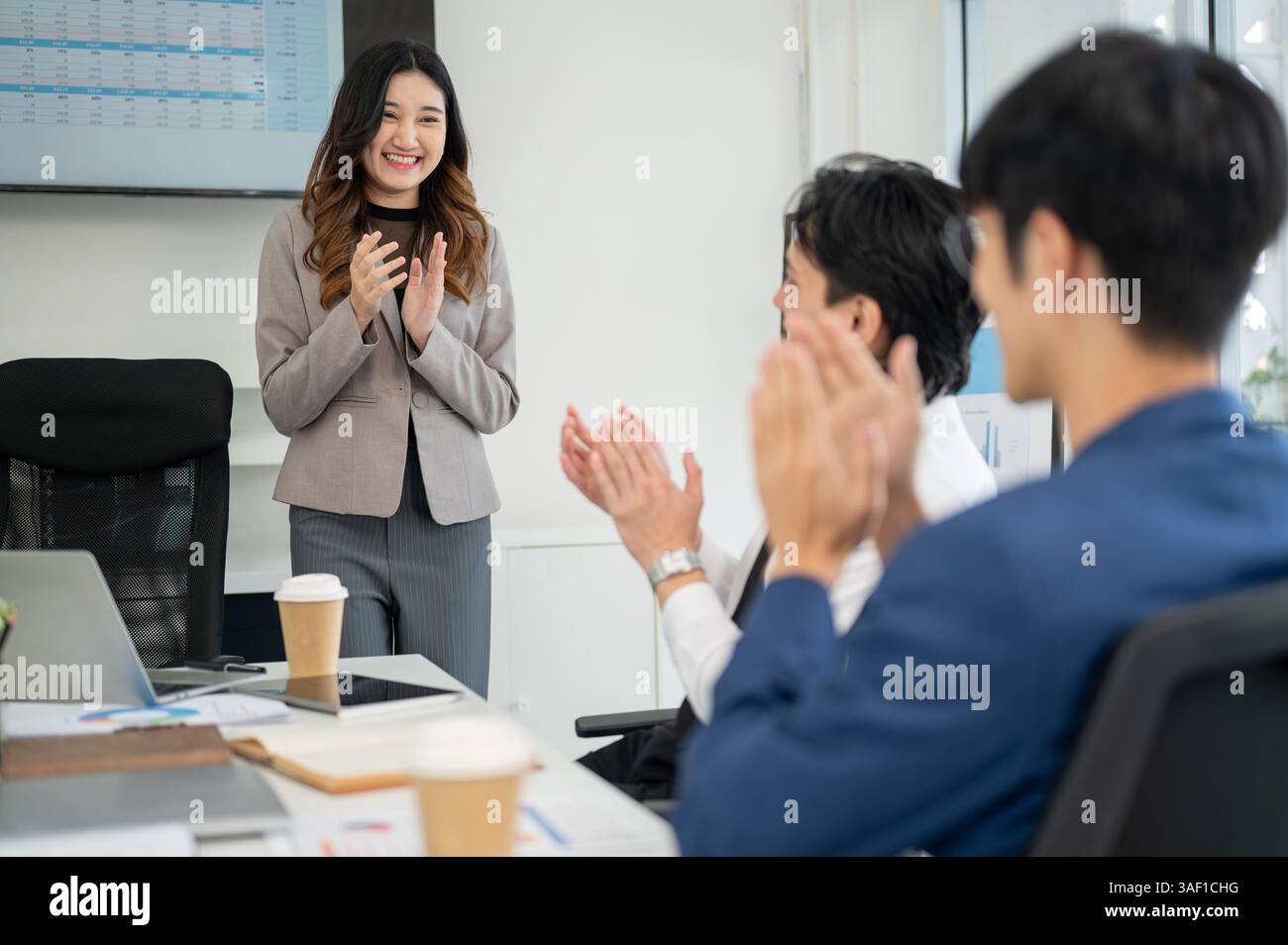 Female office worker is smiling while standing and clapping her hands ...