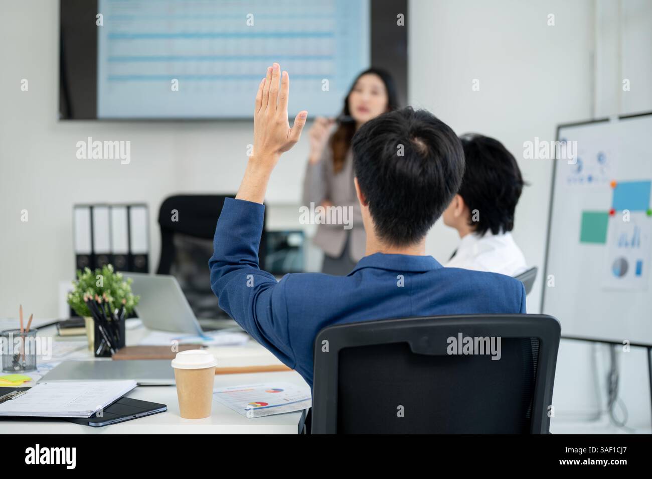 Male office worker is raising a hand to ask a question with his female ...