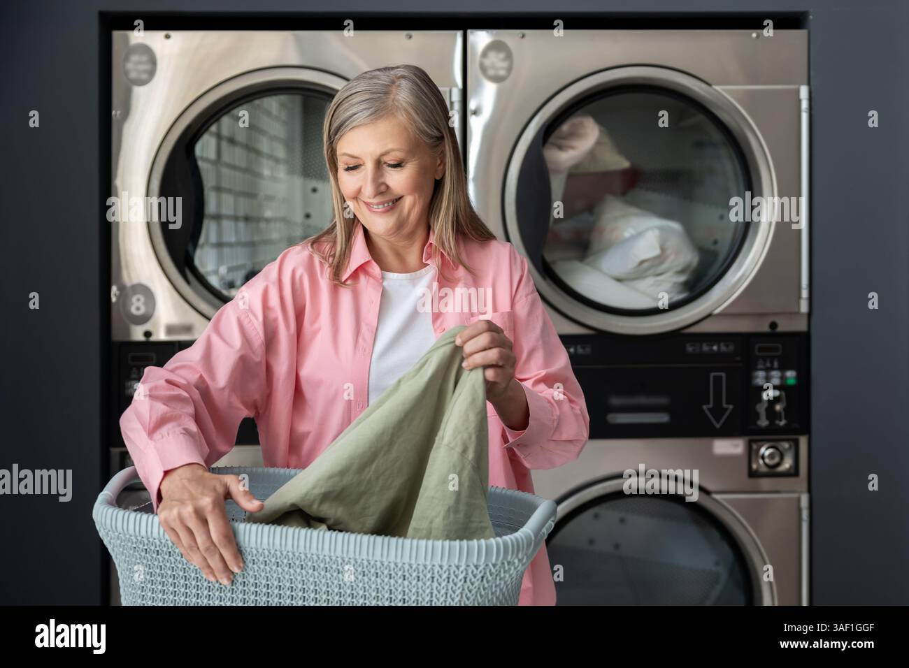 Mature woman in laundromat using industrial washing machines and dryers ...