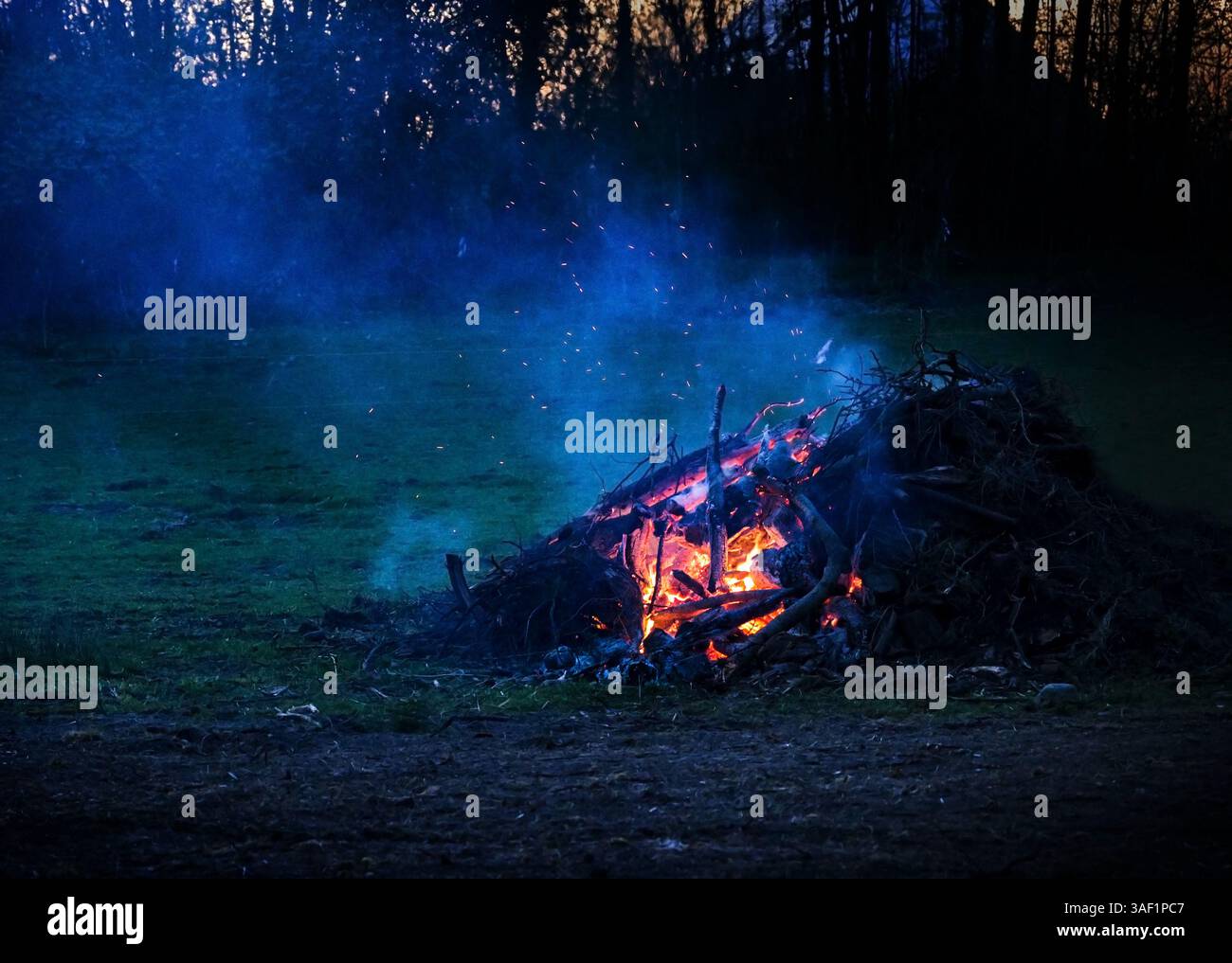 Burning heap from tree cuttings in the night with ember, smoke and ...