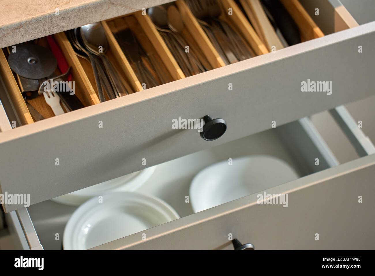 Modern kitchen with dishes and cutlery in open drawers. Contemporary kitchen cabinets. Concept ...