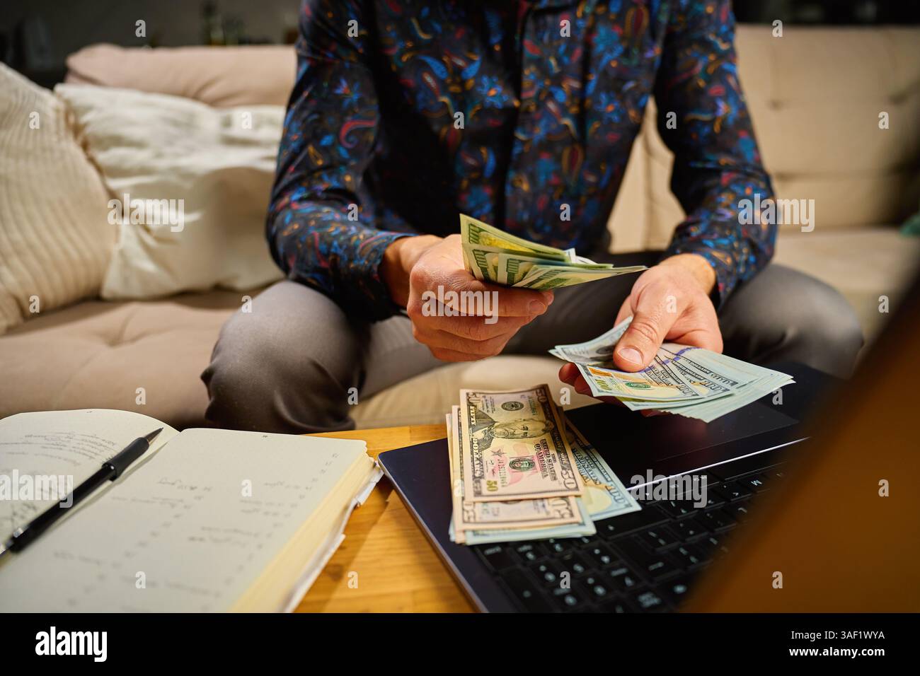 Man holding dollar banknotes, sitting on sofa in front of table with ...