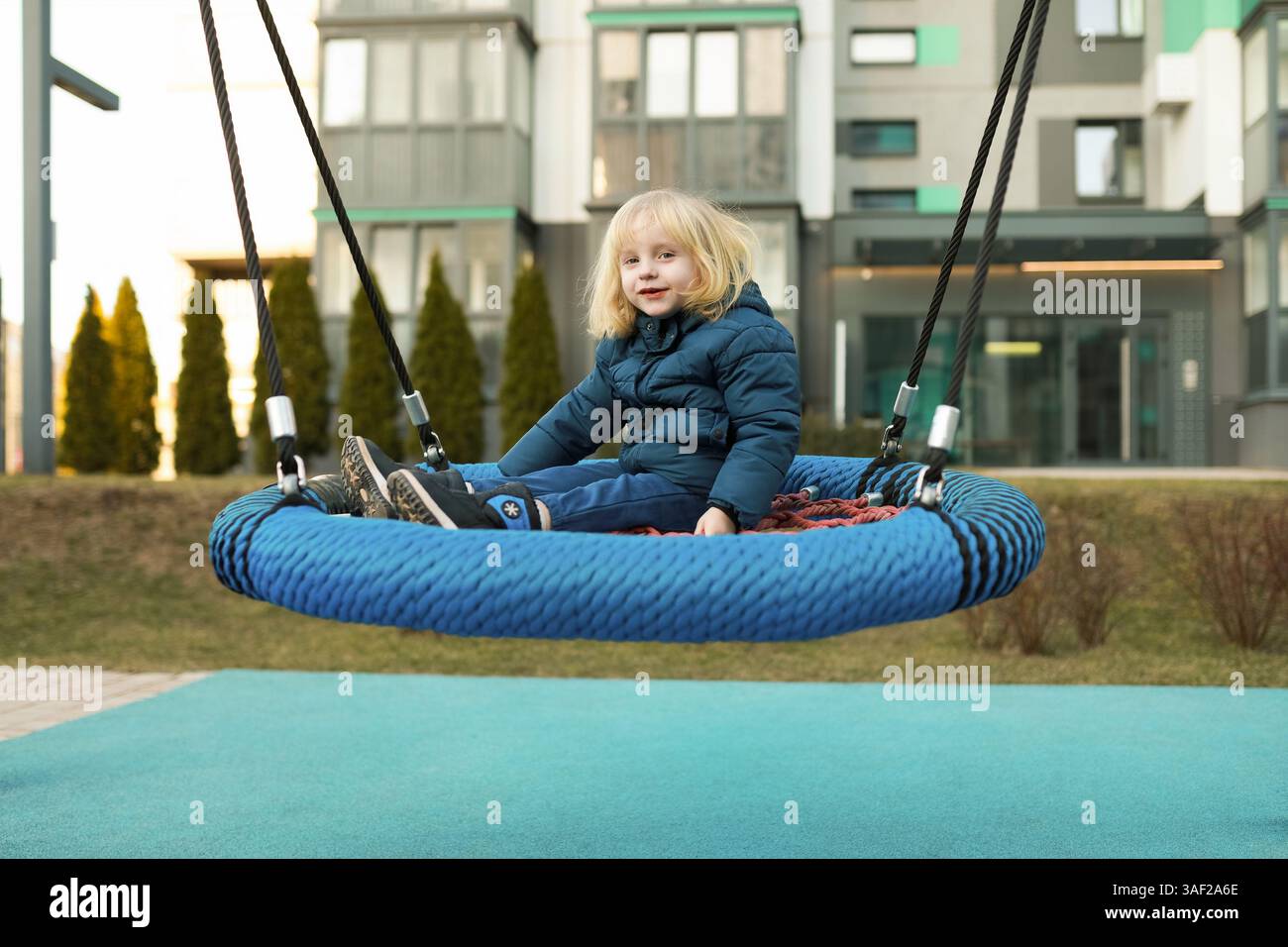 Child enjoys swinging on a circular swing in a modern playground during ...