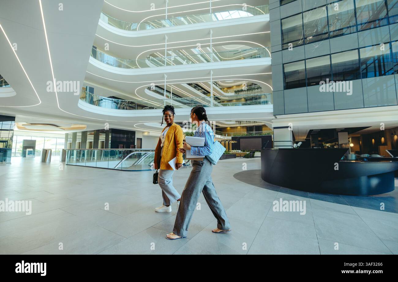 Two female corporate professionals walk and converse in a spacious ...