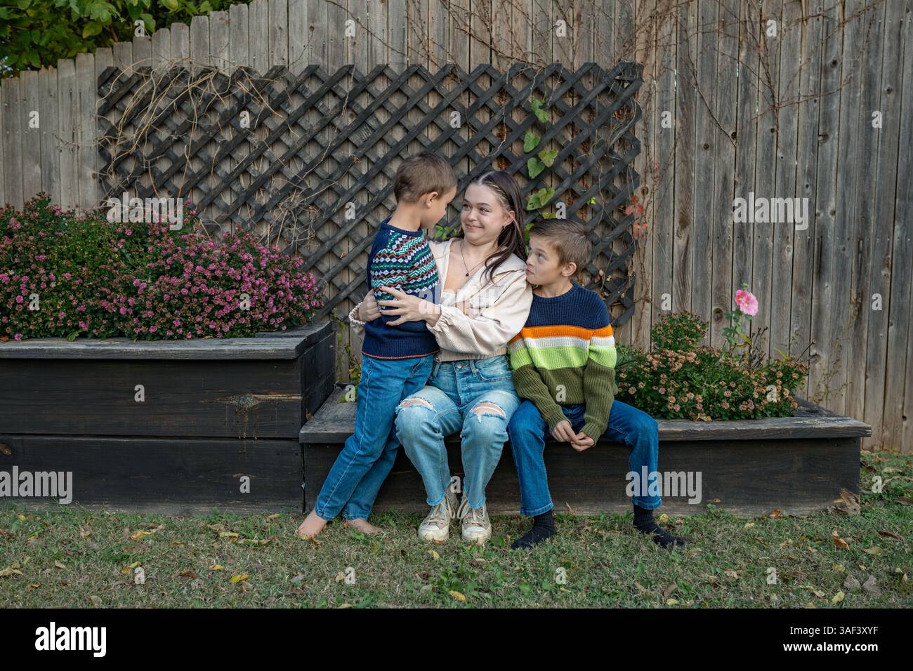 Three siblings sitting on a wooden bench, laughing and interacting ...