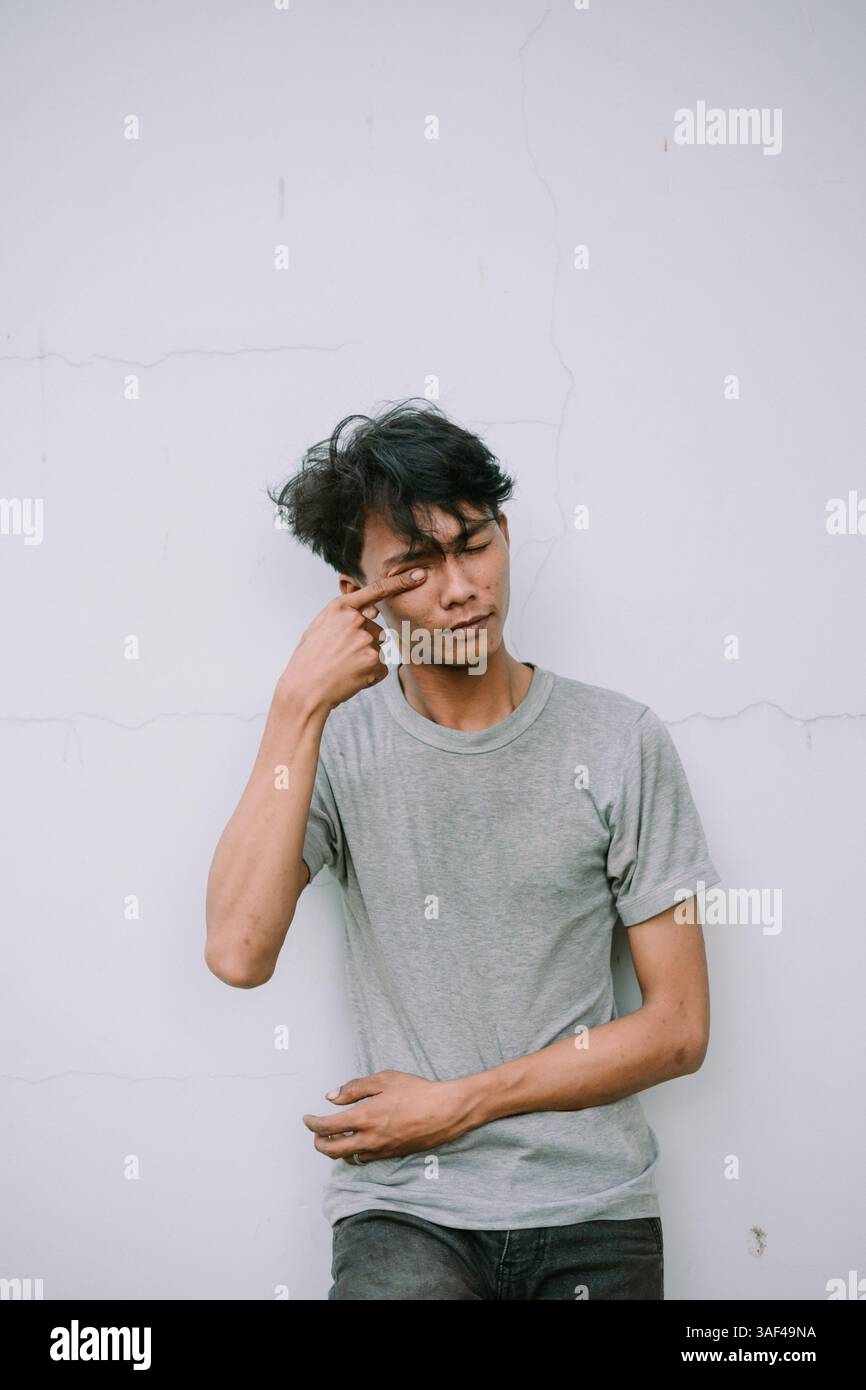 Pensive asian man touching his eye against a white textured backdrop ...