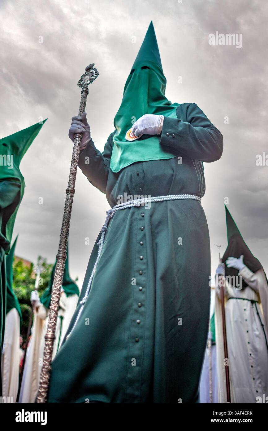 A Nazareno dressed in traditional robes and capirote holds a ...