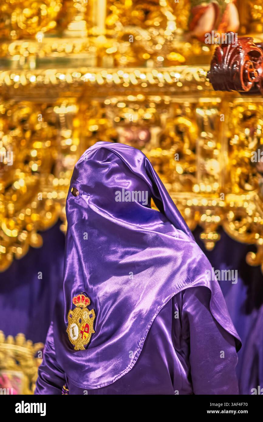 A penitent in a purple robe stands beside the intricately decorated ...