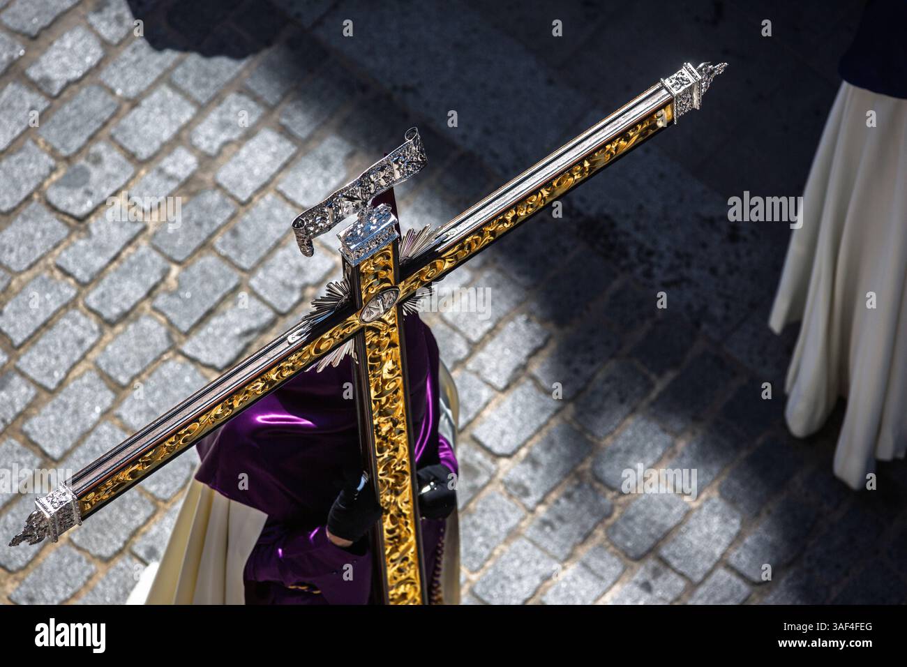 Hooded penitent holding golden adorned cross during Holy Week ...