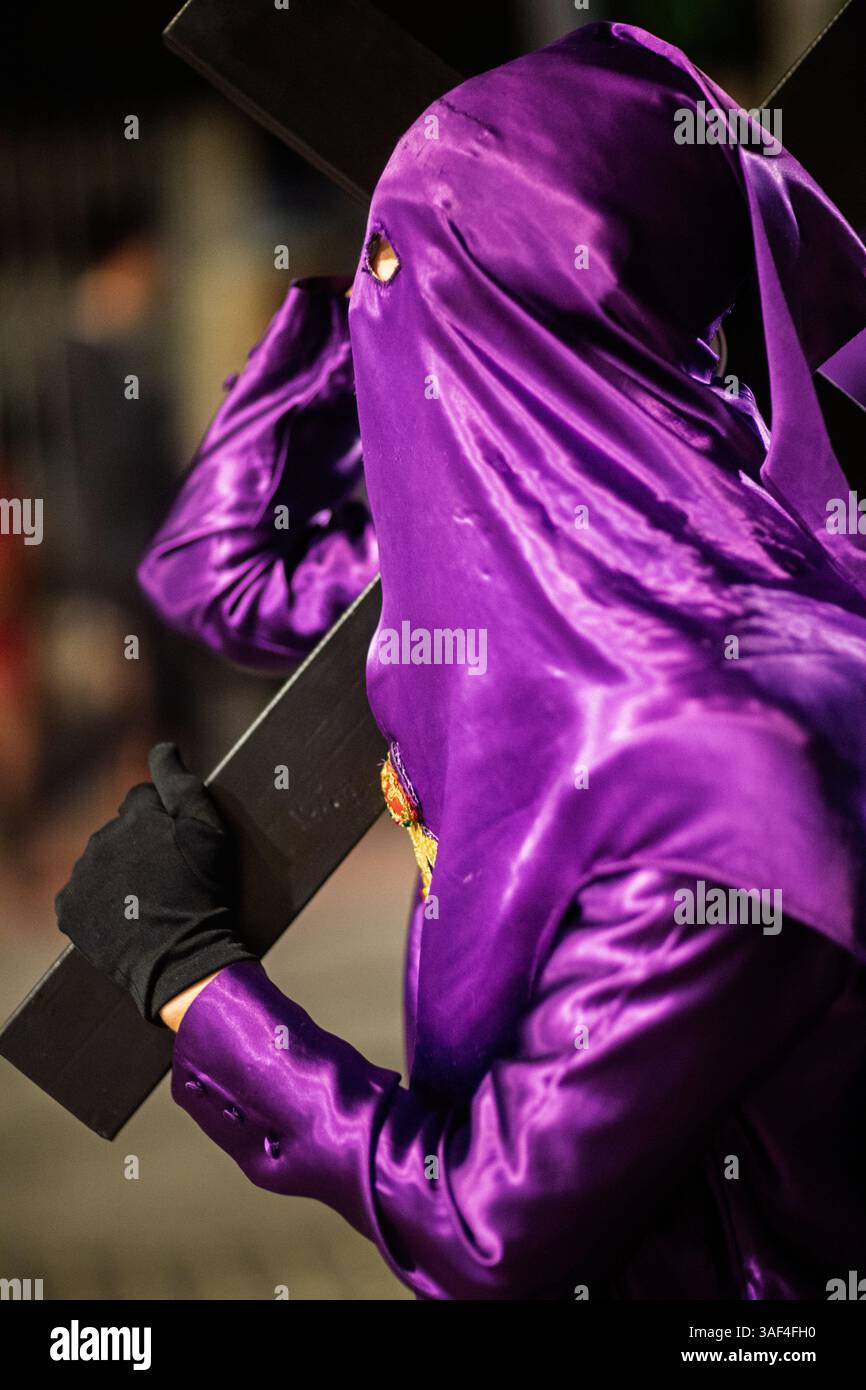 Hooded penitent in purple robes carries a large cross during an Easter ...