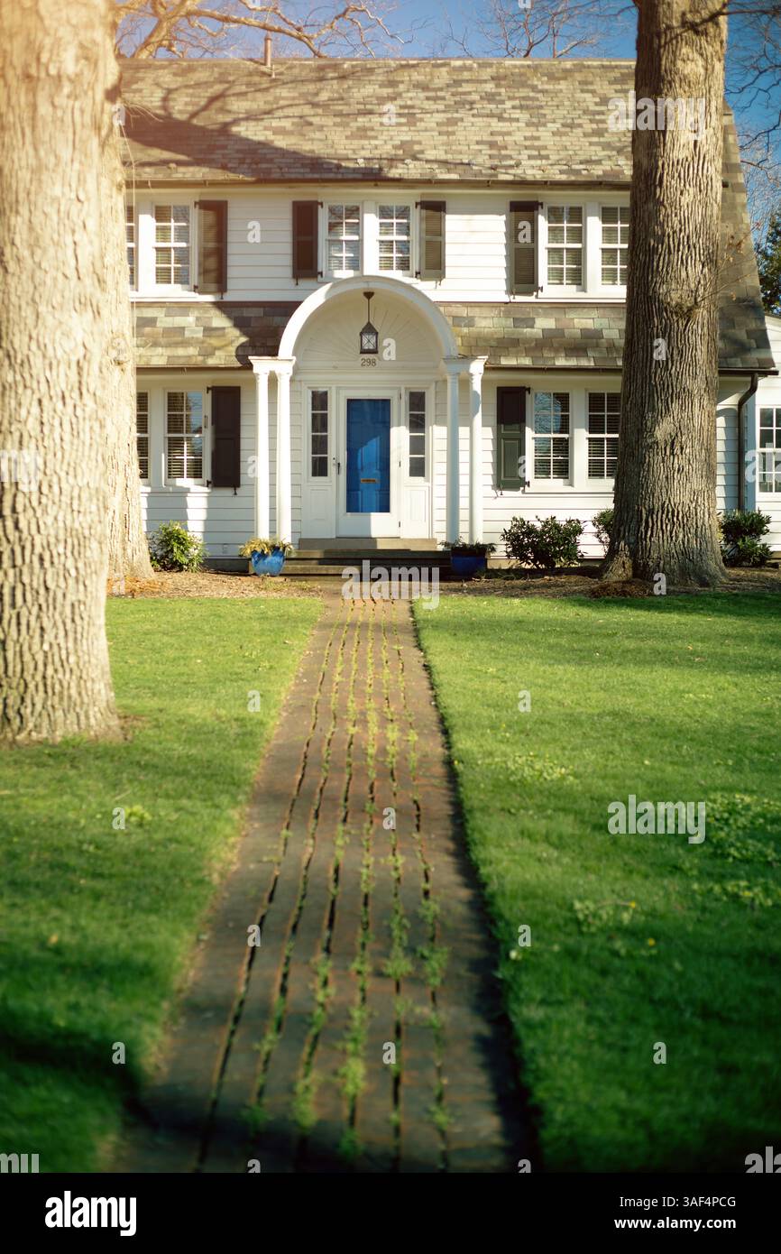 White two-story house with dark shutters in a long green lawn area ...