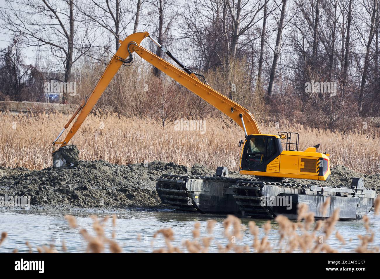 Amphibious excavator dredging riverbank and moving mud with long ...