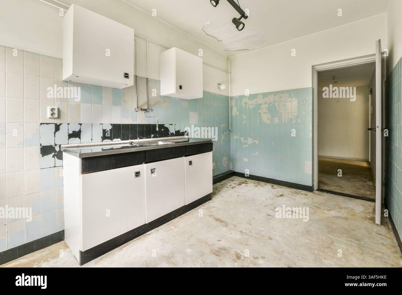 An abandoned kitchen showcasing peeling paint and faded blue tiles ...