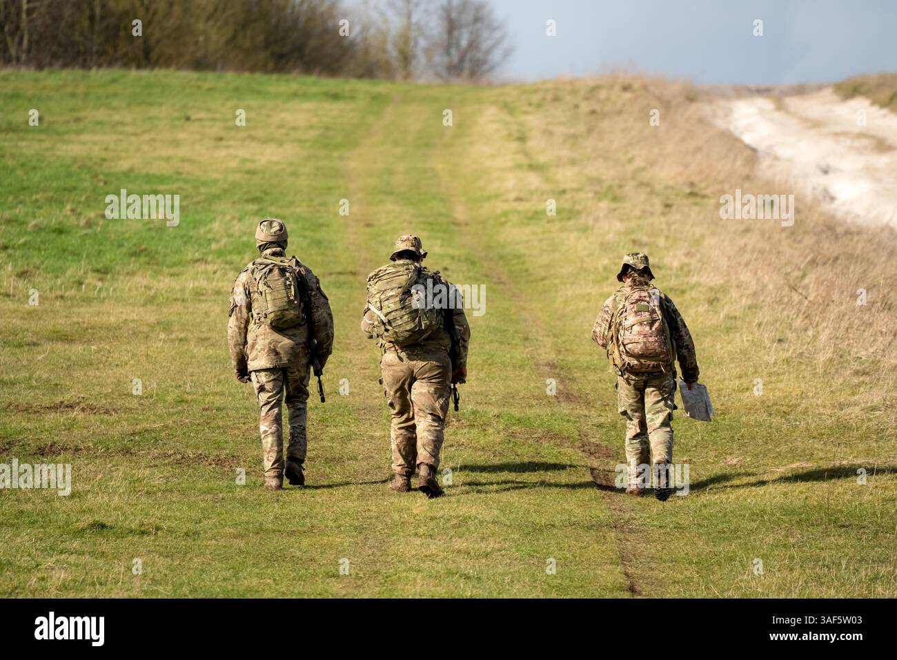 2 male and 1 female soldiers tabbing with 25Kg bergens in countryside ...