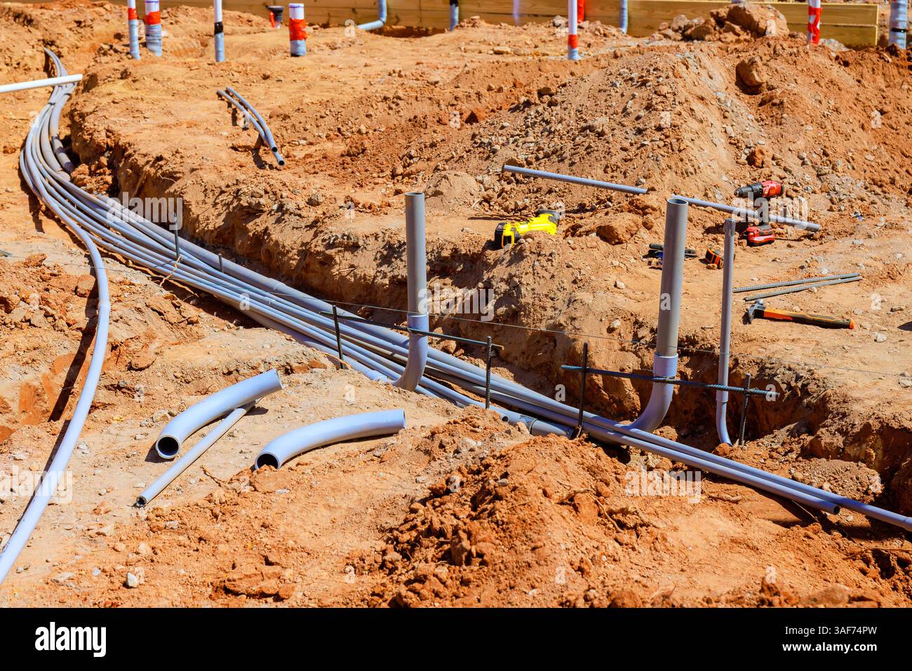 Workers are laying out electrical pipes in trench at construction site ...