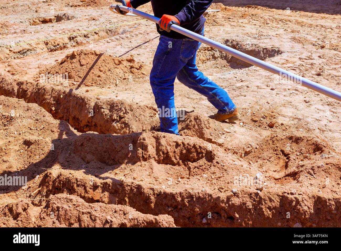 Worker laying out electrical pipes to shape sandy ground during ...