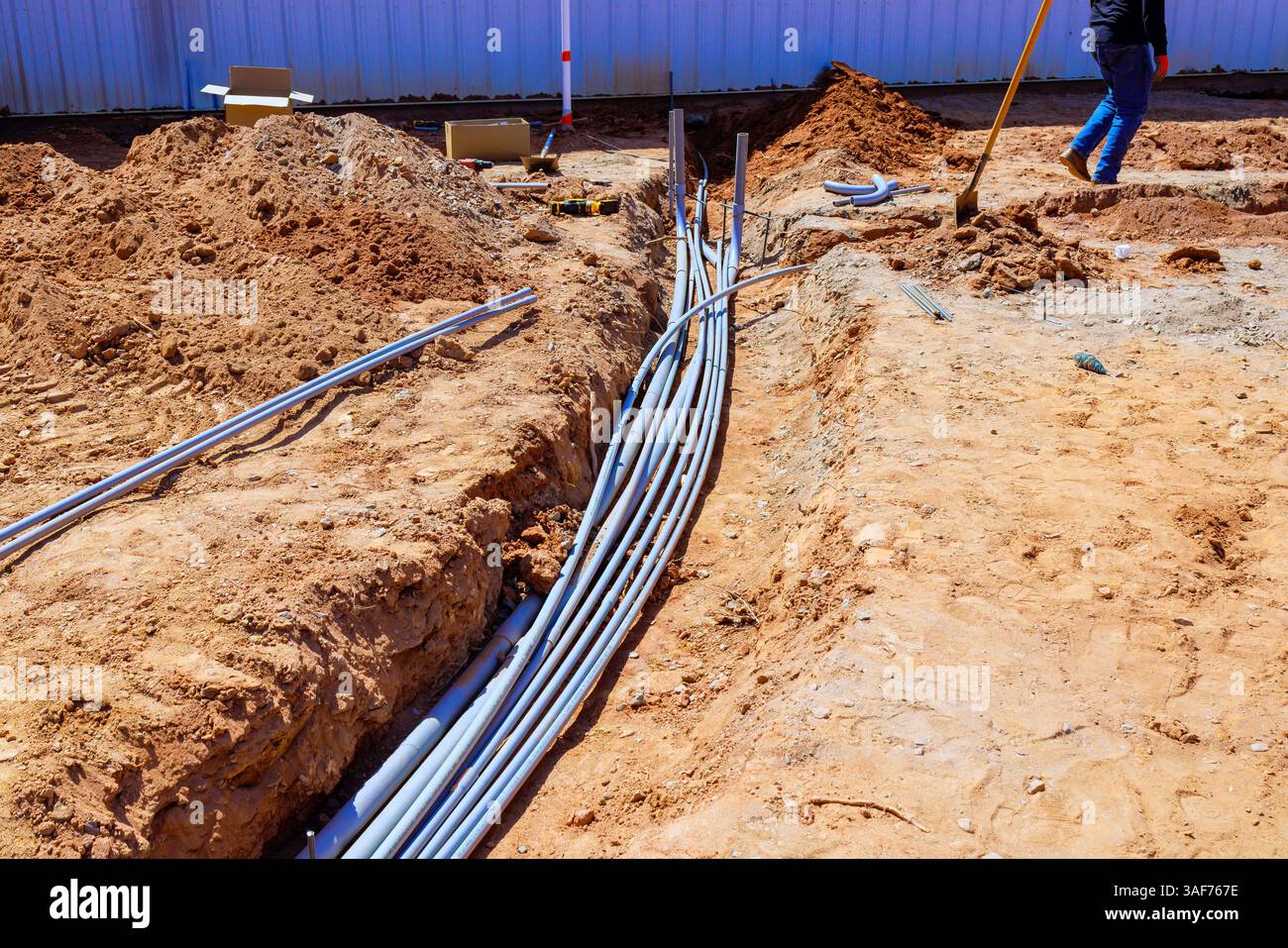 Workers organize electrical conduits in trench at construction site ...