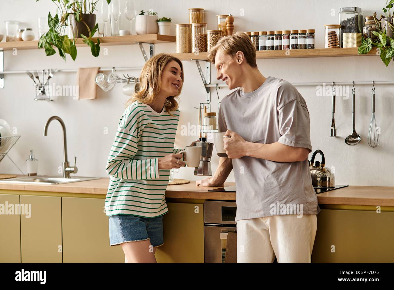 A young couple shares laughter and coffee in their modern kitchen ...