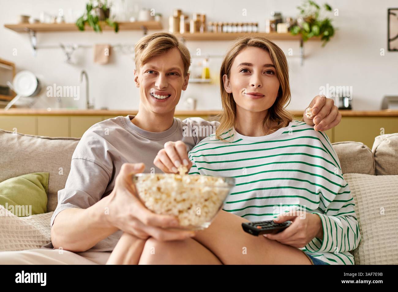 A young couple cuddles on the couch, sharing popcorn and laughter ...