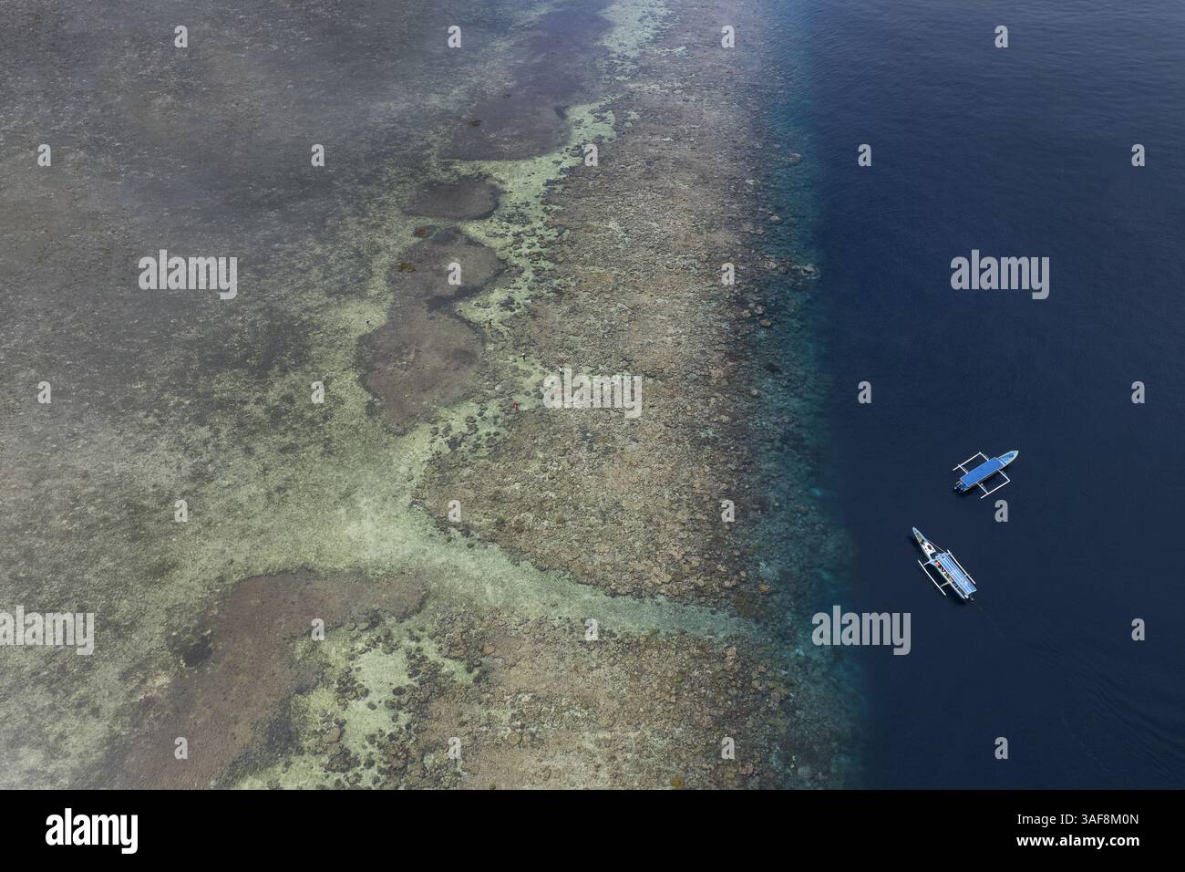 Two fishing boat anchored at the edge of vast coral reef during low ...