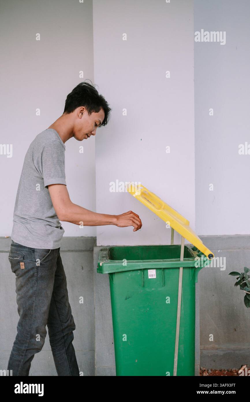 Young man putting trash into green recycling bin. Daily activity for ...