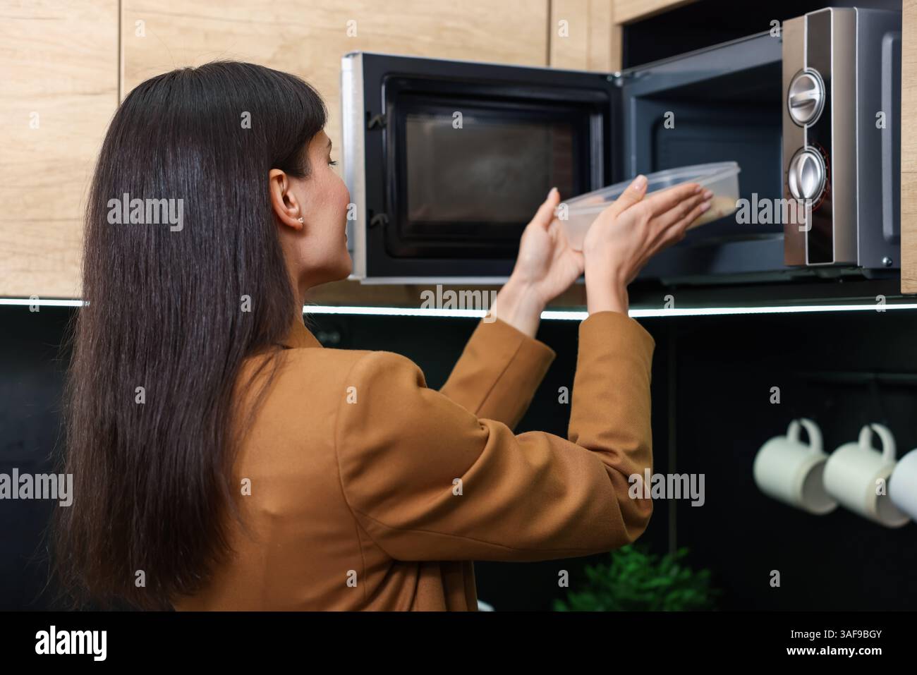 Woman putting container with lunch into microwave indoors Stock Photo ...
