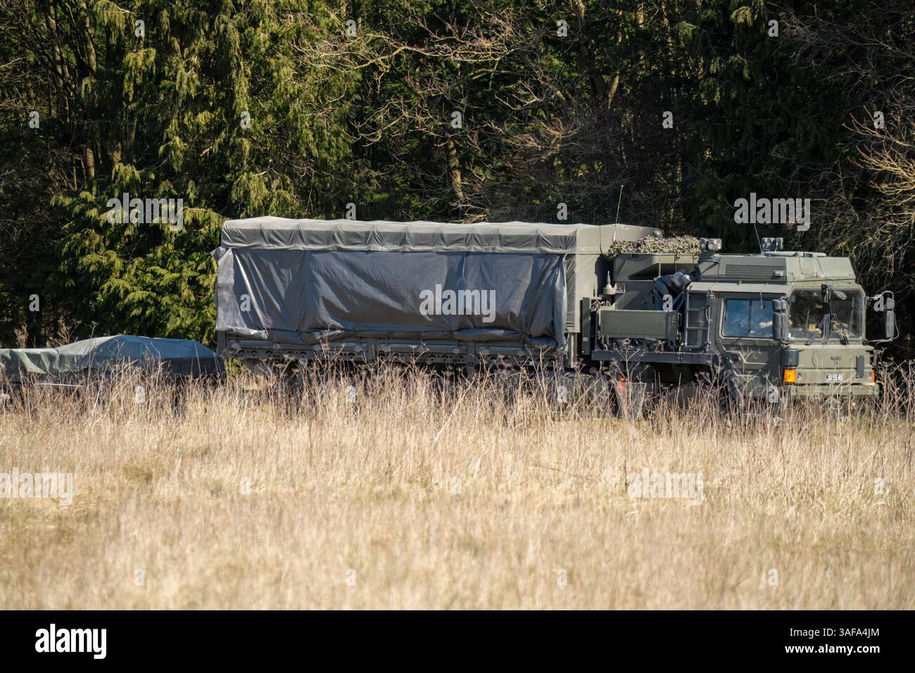 British army MAN HX 6x6 utility truck with trailer moving along a dirt ...