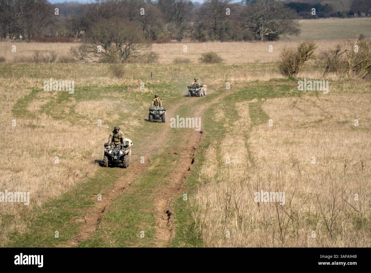 a convoy of army soldiers riding quad bikes, driving across countryside ...