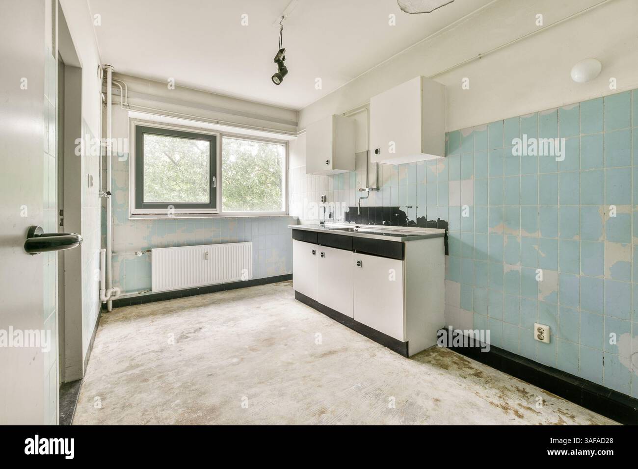 An empty kitchen space with faded blue tiles and simple cabinetry ...