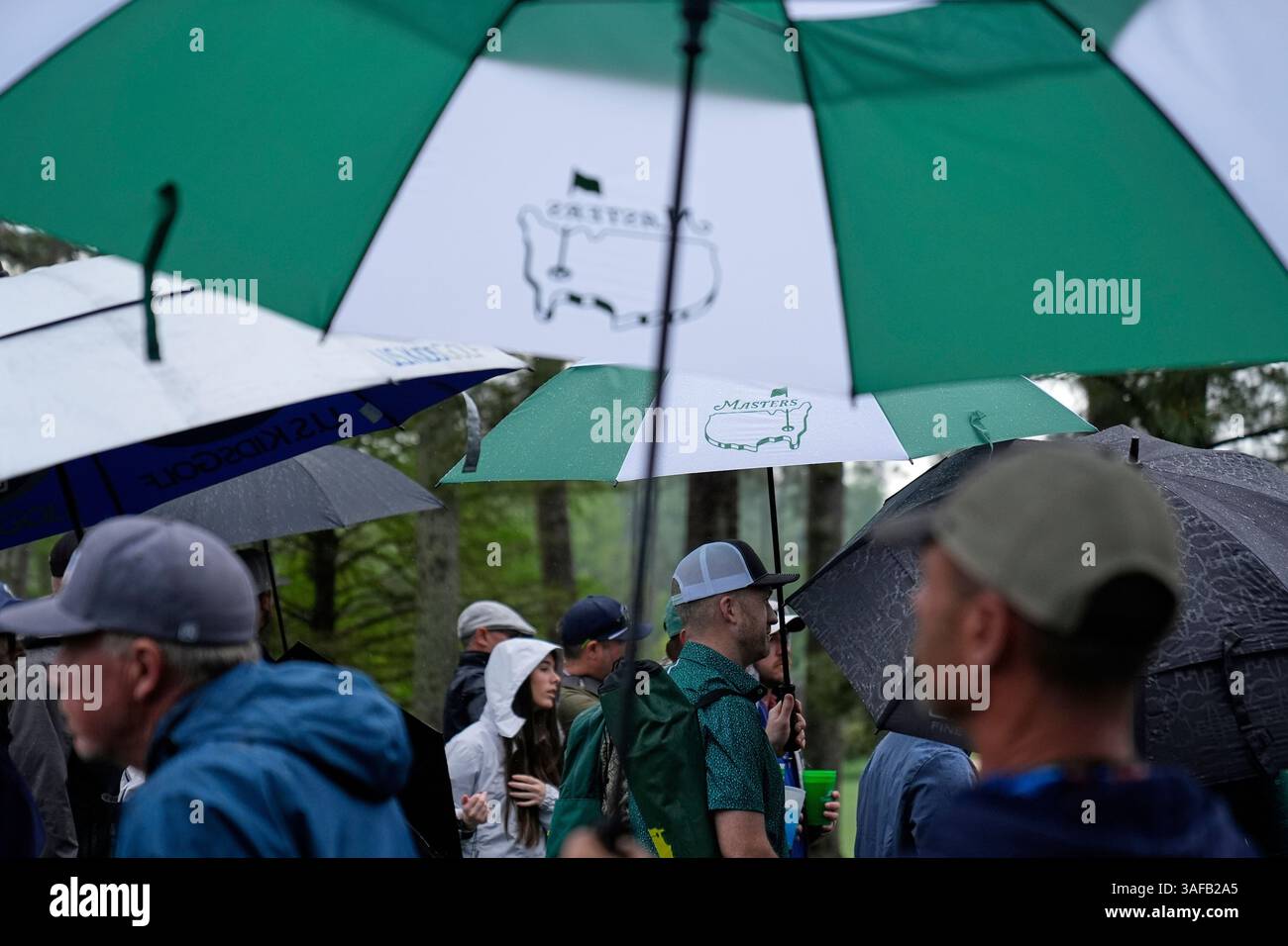 Patrons walks under umbrellas along the 13th green during a practice ...