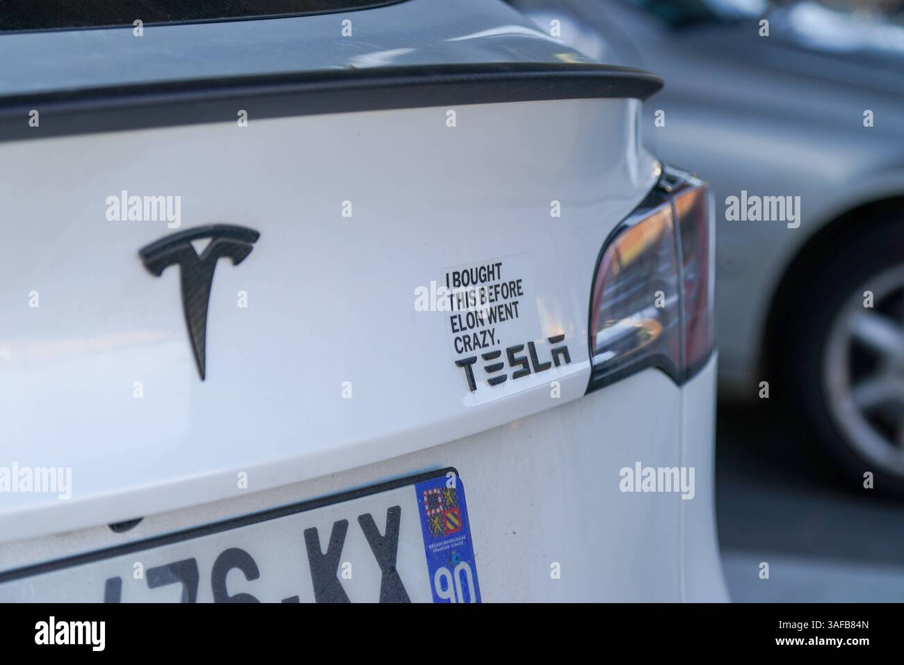 Auf dem Heck eines weißen Tesla-Fahrzeugs ist ein auffälliger Sticker ...