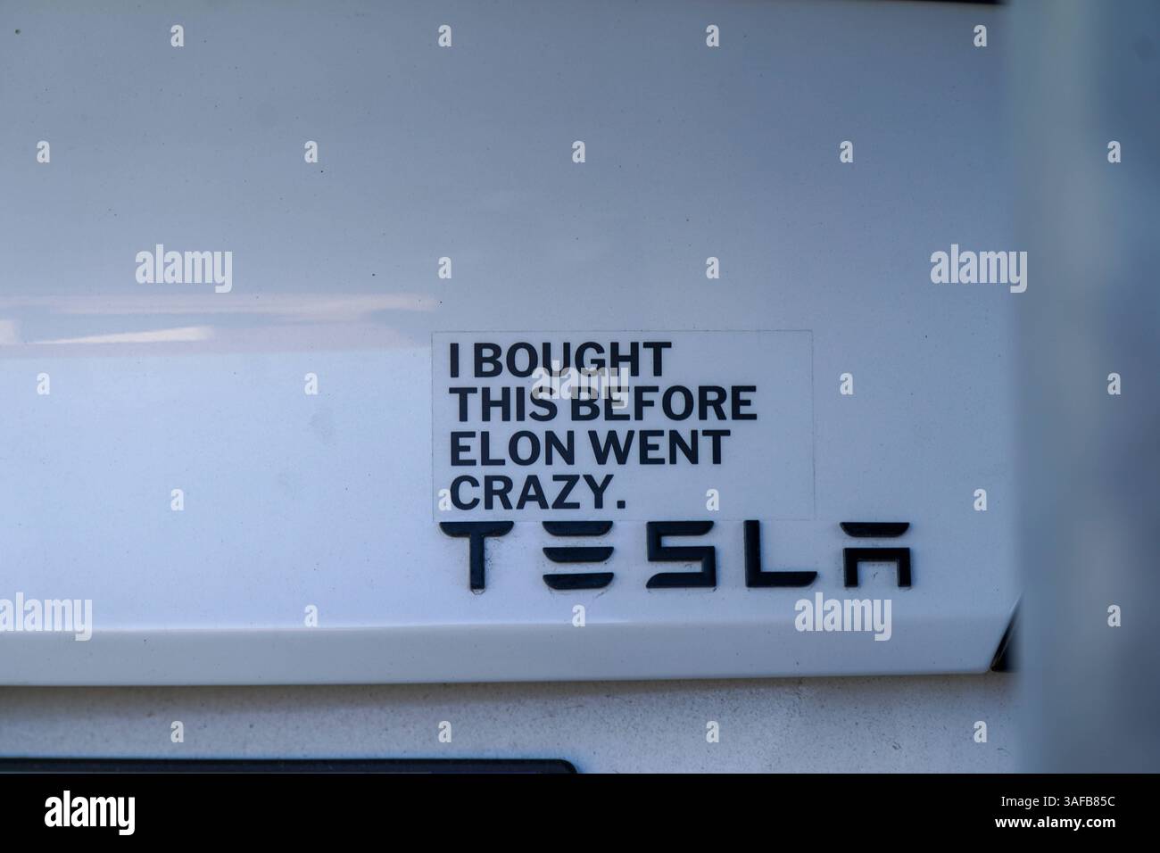 Auf dem Heck eines weißen Tesla-Fahrzeugs ist ein auffälliger Sticker ...