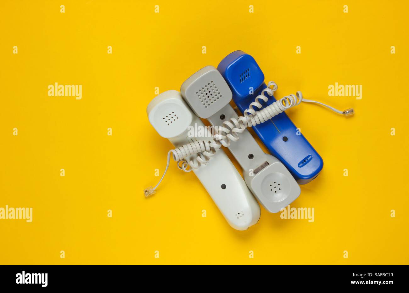 Three office phone tubes wrapped in cable on yellow studio background ...